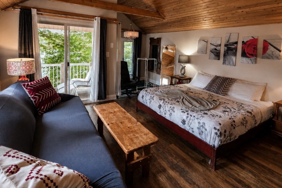 Um quarto acolhedor com teto de madeira, cama com roupa de cama floral, sofá com almofadas estampadas e um banquinho.