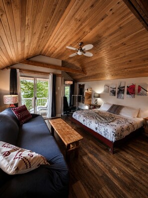 Um quarto acolhedor com teto de madeira, cama com roupa de cama floral, sofá com almofadas estampadas e um banquinho.