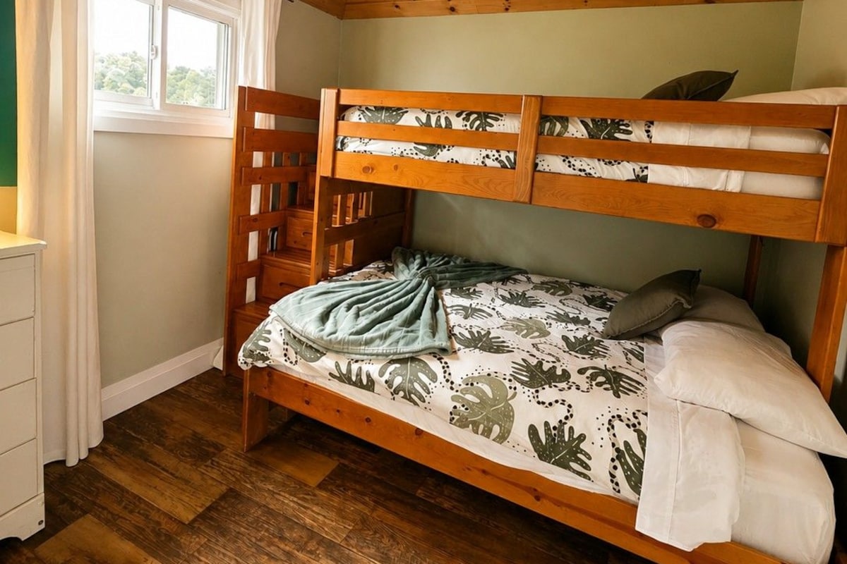 Quarto com beliche, teto de madeira e janela com cortinas.