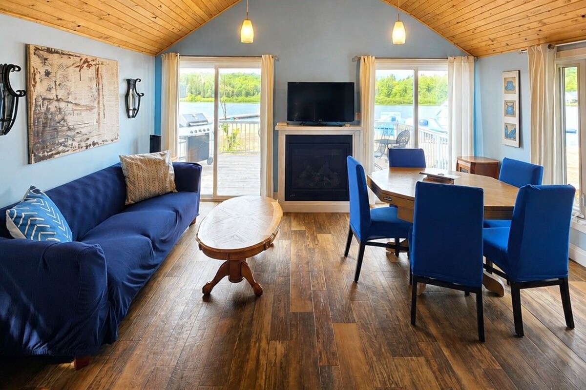 Uma sala de estar ampla com teto de madeira, lareira, televisão e mesa de jantar com cadeiras azuis.