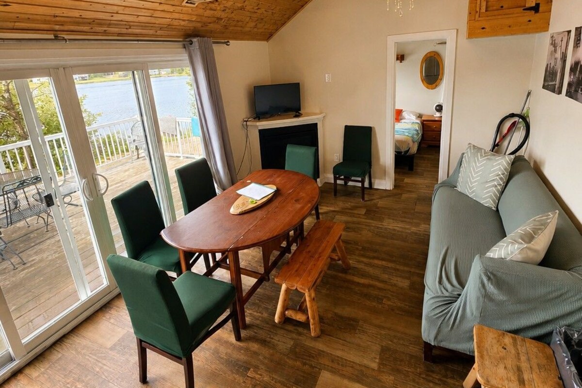 Uma sala de estar acolhedora com teto de madeira, lareira, sofá e mesa de jantar com cadeiras.