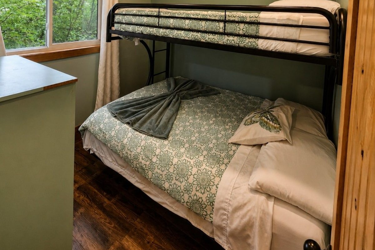 Uma cama de beliche com escrivaninha e janela em quarto com vigas de madeira no teto.