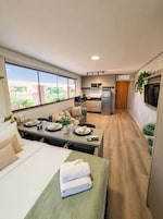 Quarto de hotel moderno com área de refeições, cozinha compacta e uma grande janela com vista para o exterior.