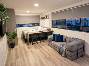 Apartamento moderno com área de refeições, sofá e grande janela com vista para a cidade.