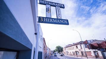 Vista da rua com placa indicando 'RESTAURANTE HOSTAL 3 HERMANOS' e um edifício com entrada visível.