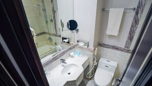 Casa de banho com chuveiro em cabine de vidro, pia com espelho, sanita e porta-toalhas.