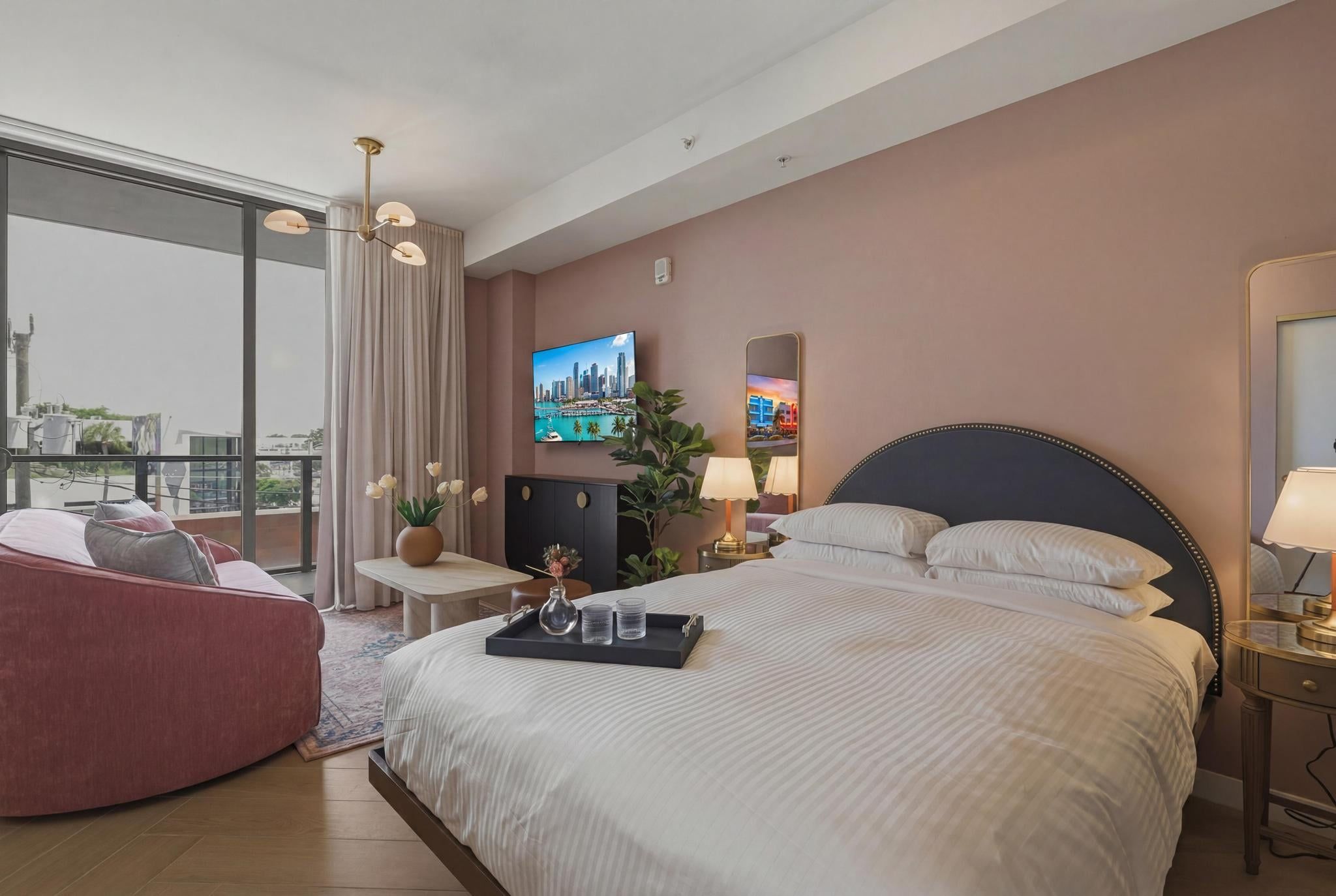 Quarto de hotel moderno com uma cama grande, televisão, escrivaninha e varanda com vista para a cidade.