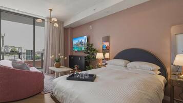 Quarto de hotel moderno com uma cama grande, televisão, escrivaninha e varanda com vista para a cidade.