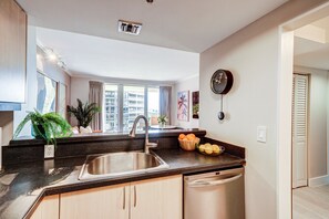 Cozinha moderna com pia de aço inoxidável, bancada de madeira e vista da cidade através de amplas janelas.