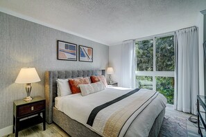 Quarto com uma cama grande, duas mesas de cabeceira, uma janela com cortinas e duas fotos emolduradas na parede.