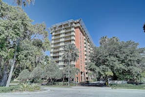 Um hotel com vários andares e varandas, cercado por vegetação exuberante e palmeiras.