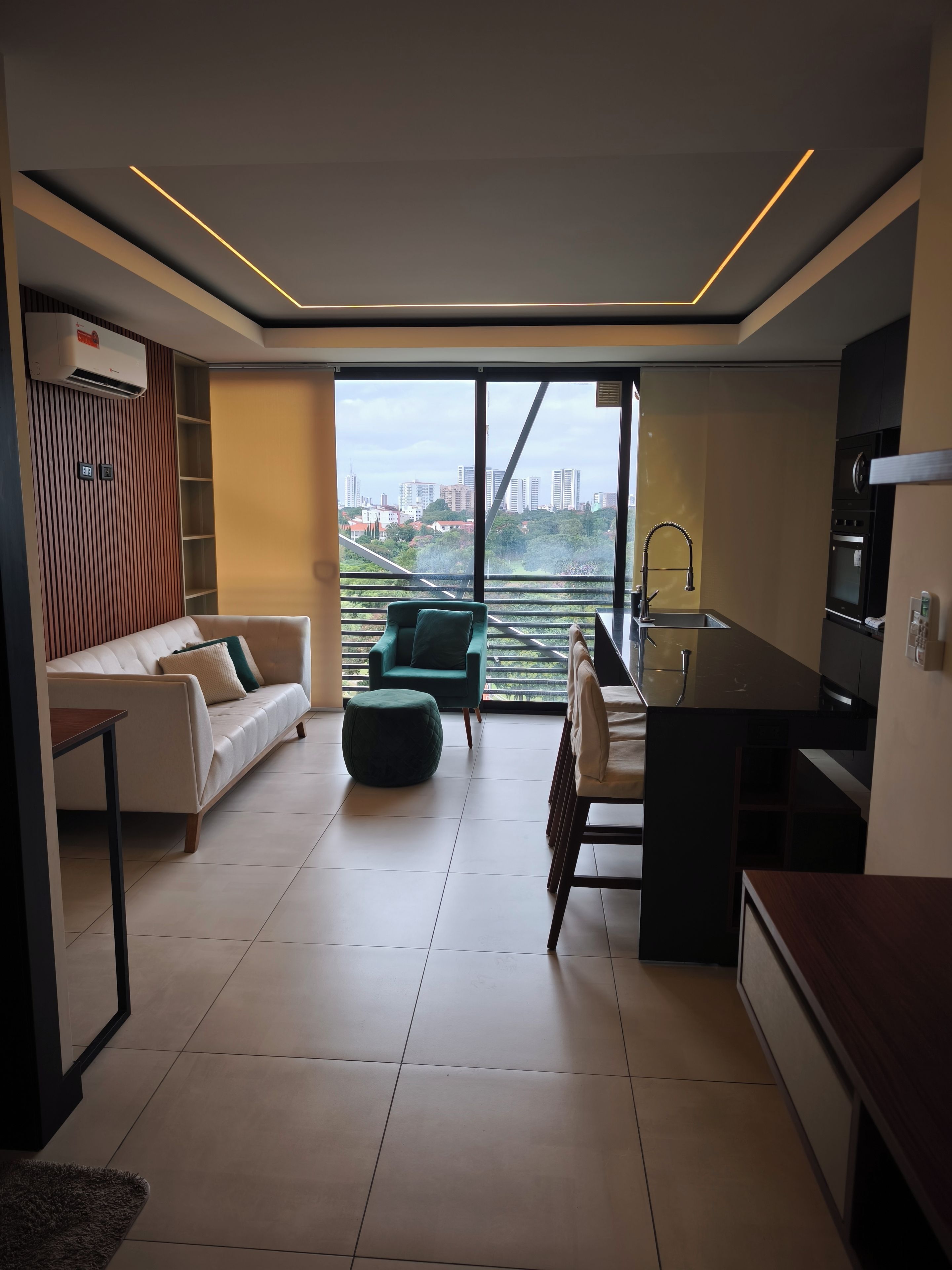 Espaço moderno com sofá, apoio para os pés e área de jantar, com vista para a cidade através de grandes janelas.
