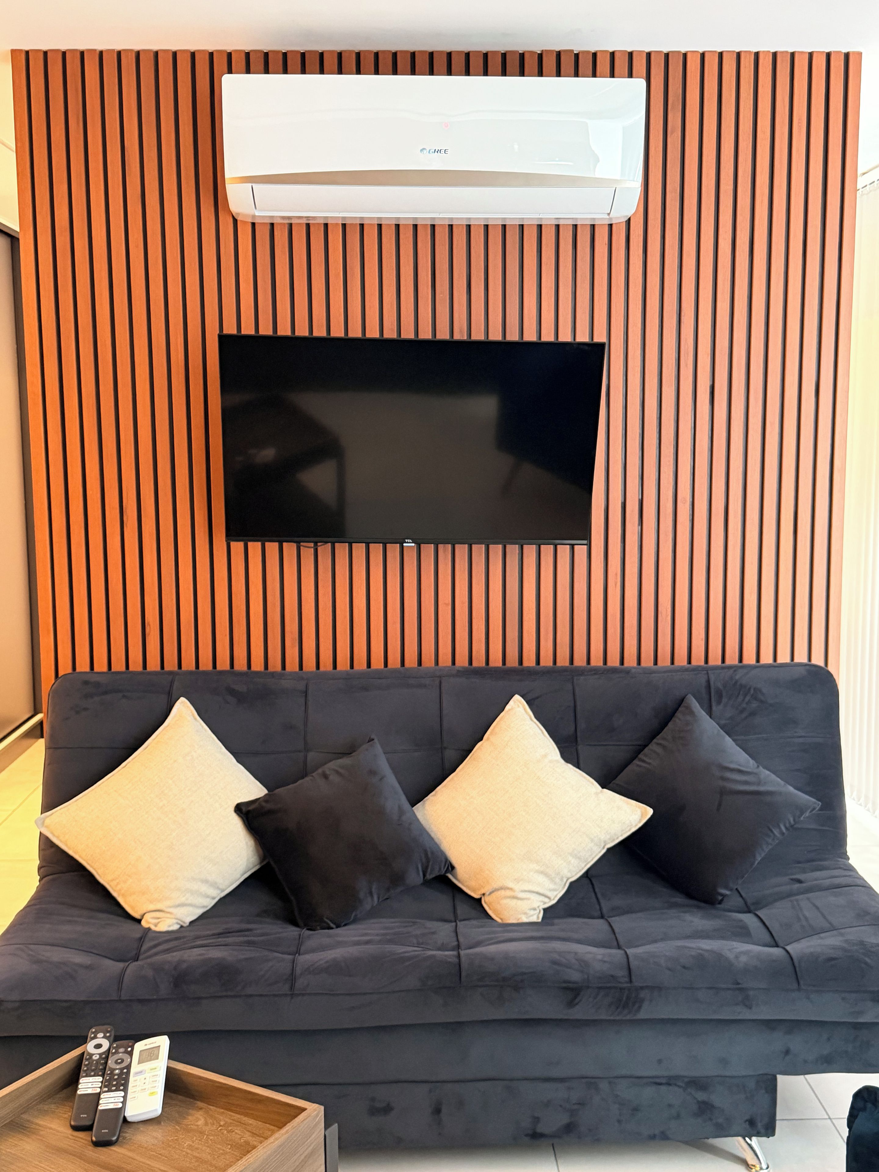 Sala de estar moderna com um sofá escuro, televisão de tela plana montada e parede de ripas de madeira.