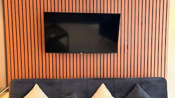 Sala de estar moderna com um sofá escuro, televisão de tela plana montada e parede de ripas de madeira.