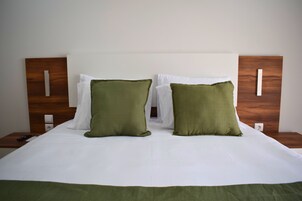 Quarto de hotel com cama, duas mesas de cabeceira e cabeceira de madeira.