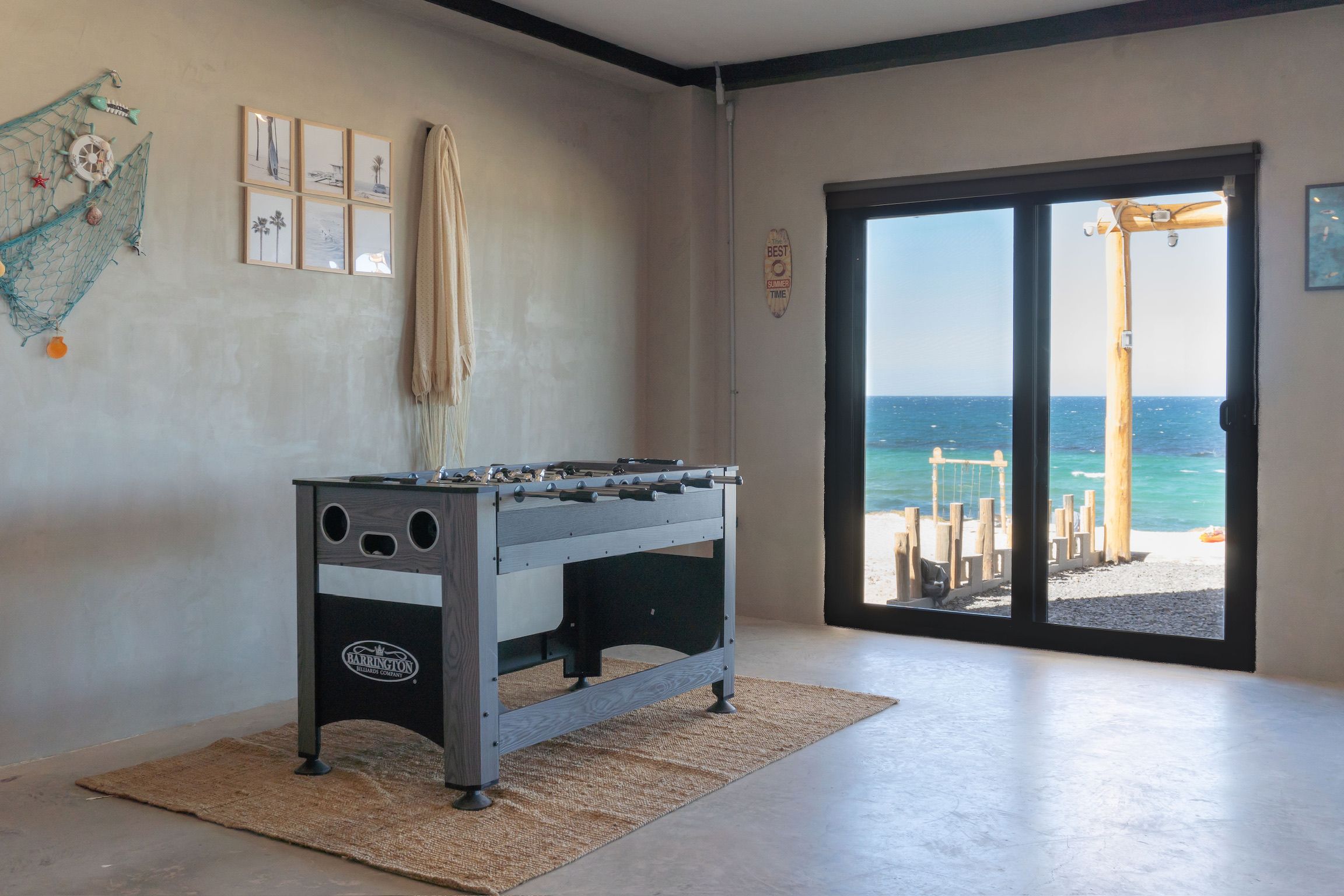 Quarto com mesa de futebol, vista para a praia através de uma porta de vidro e parede decorada com quadros e uma rede.
