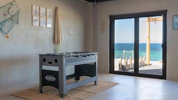 Quarto com mesa de futebol, vista para a praia através de uma porta de vidro e parede decorada com quadros e uma rede.