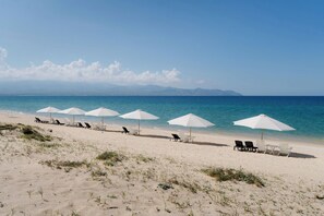 Uma praia com fileiras de guarda-sóis brancos e espreguiçadeiras.