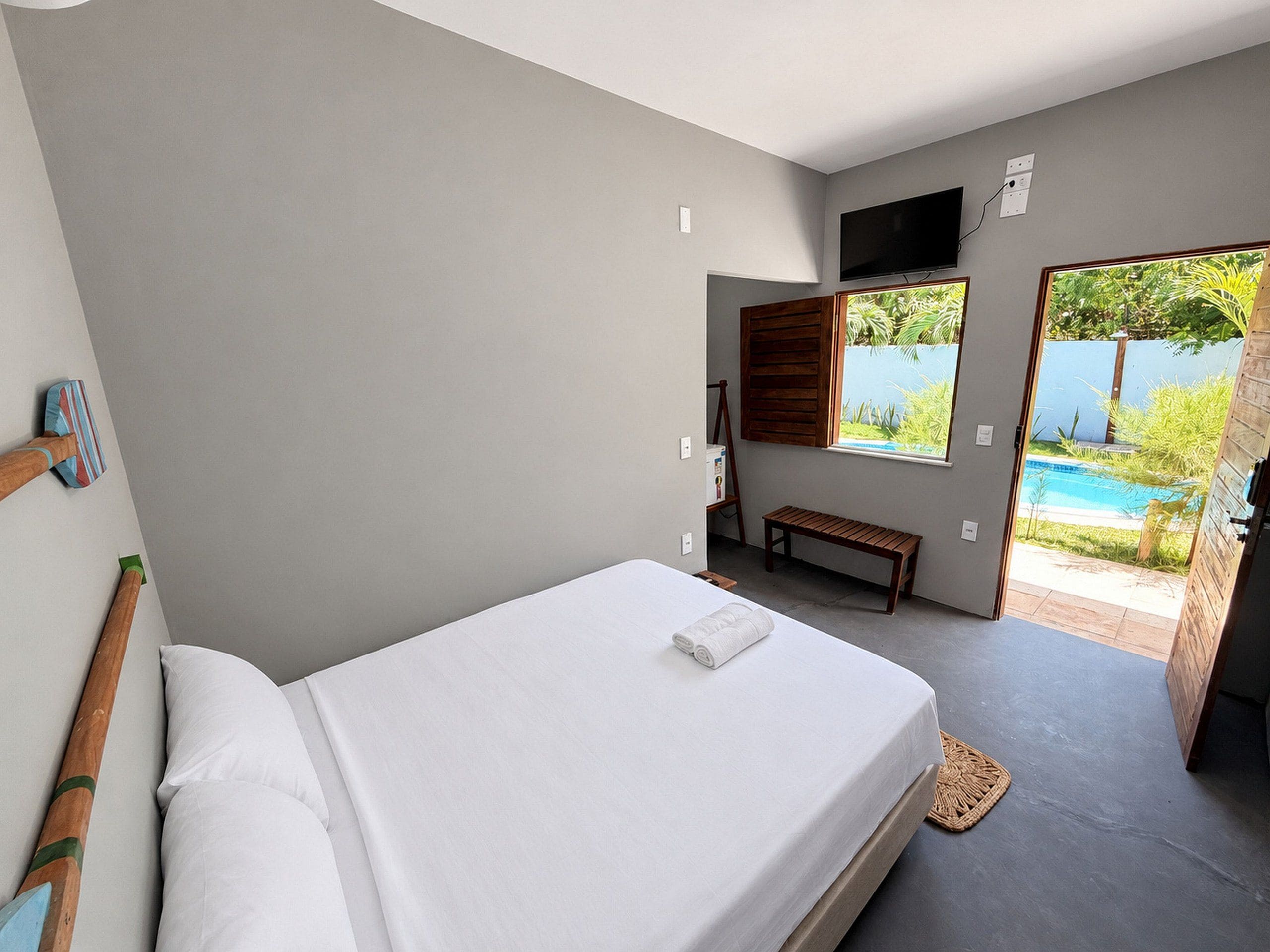 Quarto com cama, um banco, uma TV e vista para uma piscina.