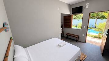 Quarto com cama, um banco, uma TV e vista para uma piscina.