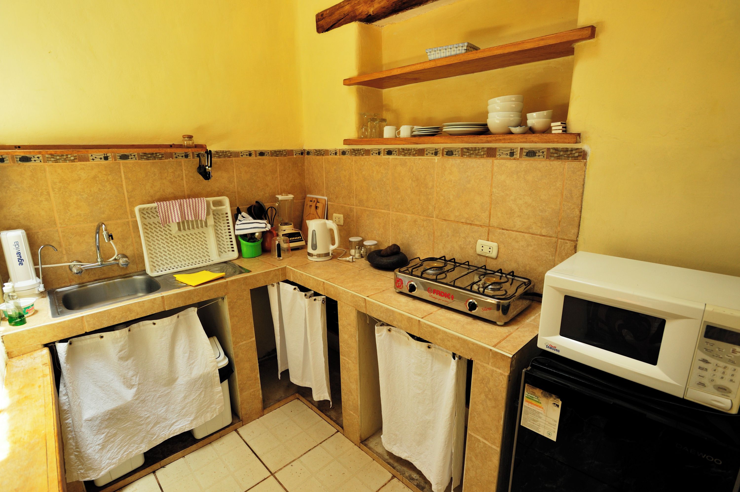 Uma cozinha compacta com pia, fogão, micro-ondas e diversos utensílios.