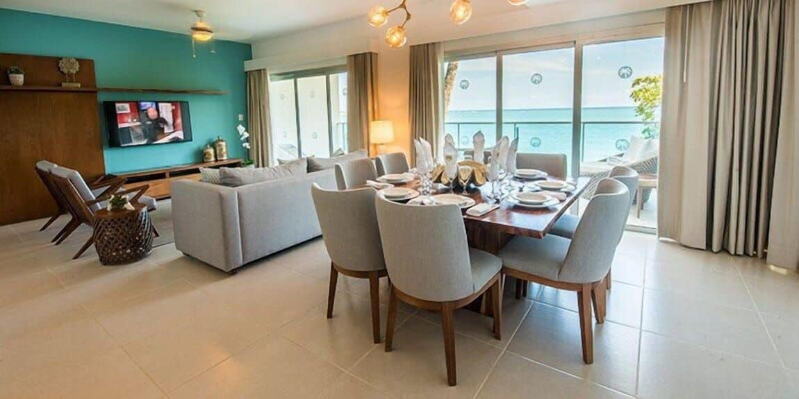Uma sala de estar moderna com área de jantar, sofá, televisão e vista para o mar.