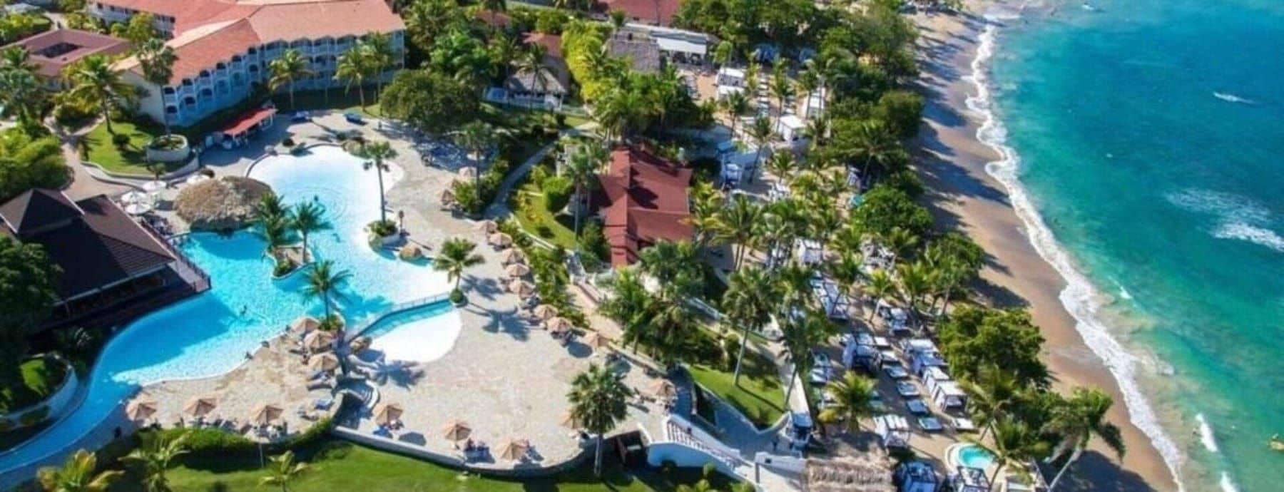 Resort com uma piscina grande, praia e palmeiras.