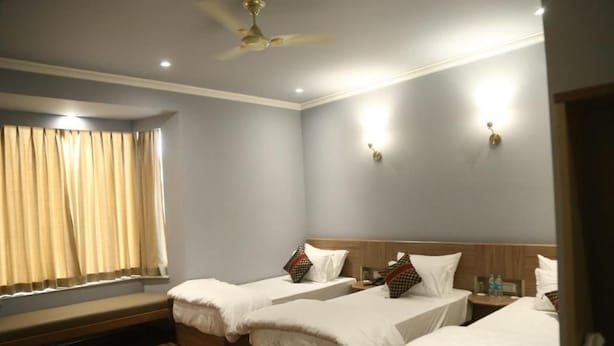 Quarto de hotel com duas camas de solteiro, um ventilador de teto, uma janela com cortinas e uma mesa de cabeceira com abajur.