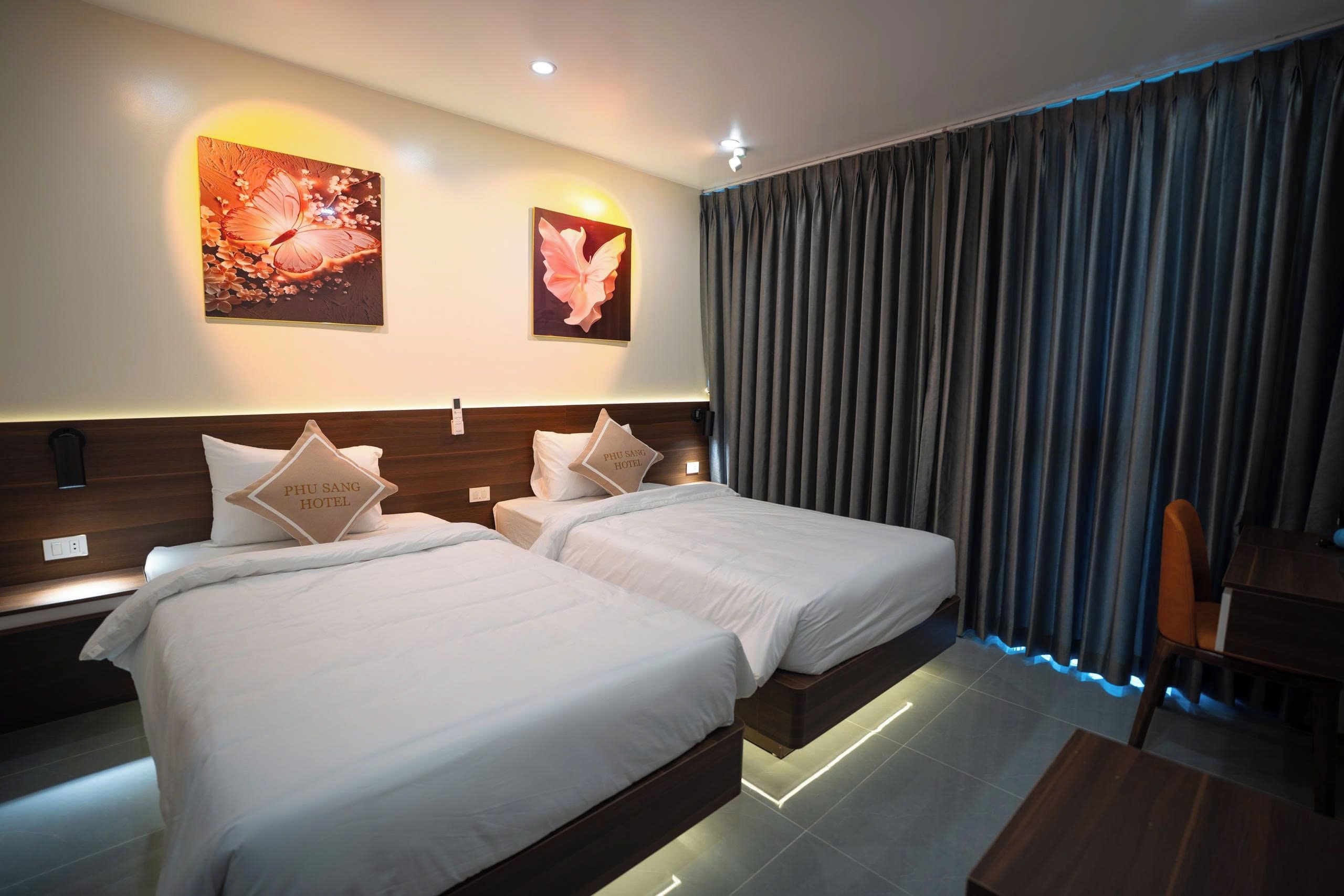 Quarto de hotel com duas camas, uma cabeceira de madeira, mesa de cabeceira, escrivaninha e uma cadeira.