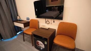Quarto de hotel com cama, televisão na parede, pequena mesa com cadeira e minibar.