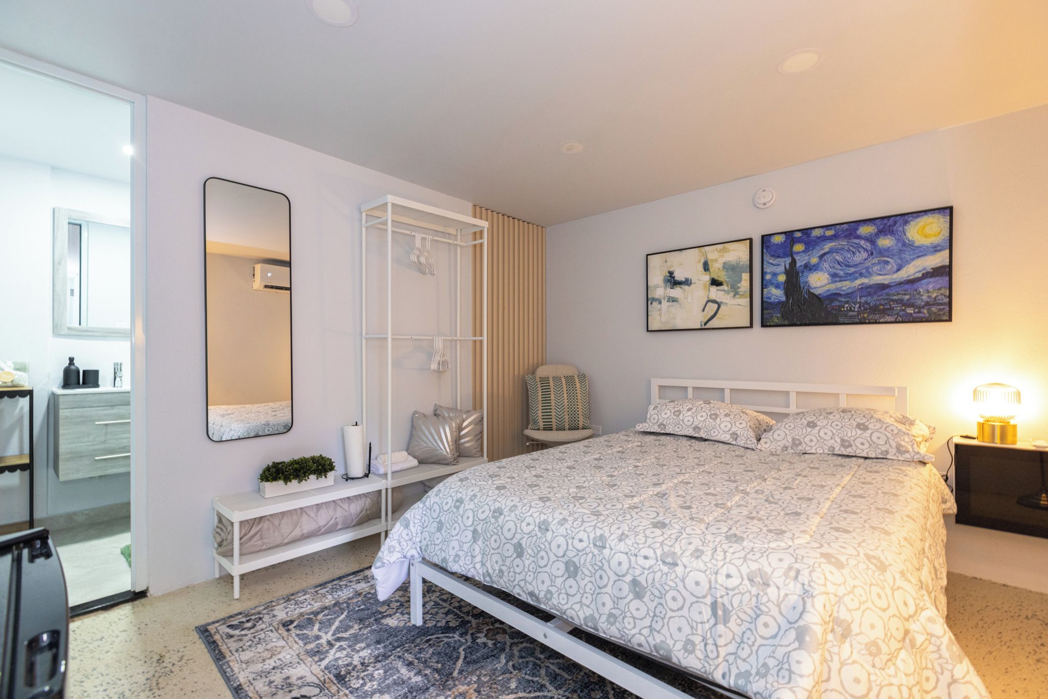 Quarto com cama, mesas de cabeceira, guarda-roupa, espelho e obras de arte na parede.