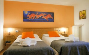 Quarto de hotel com duas camas, almofadas laranja, um quadro de coelhos e um radiador.