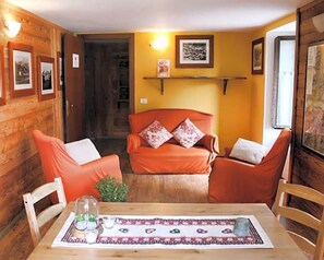 Quarto acolhedor com decoração em madeira, uma mesa de jantar com jogo de sousa e cadeiras estofadas em laranja.