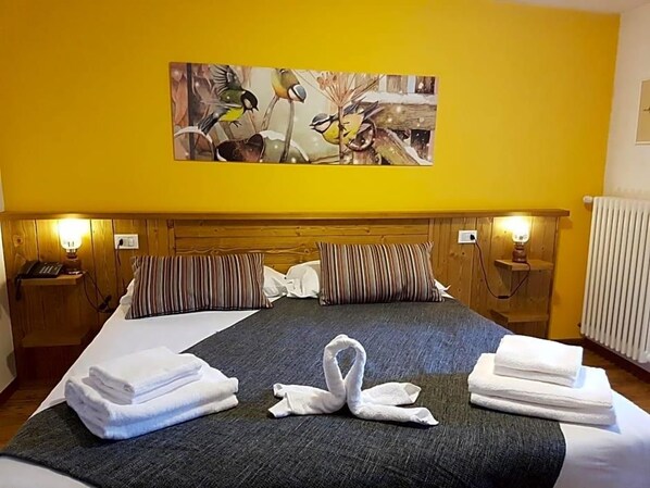 Quarto de hotel com cama, almofadas, um quadro e toalhas dispostas sobre a cama.