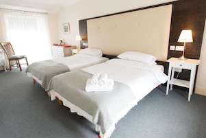 Quarto de hotel com duas camas, uma escrivaninha, uma cadeira e uma mesa de cabeceira com abajur.
