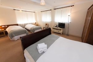 Quarto de hotel com duas camas de solteiro, uma cama grande, televisão, escrivaninha e guarda-roupa.