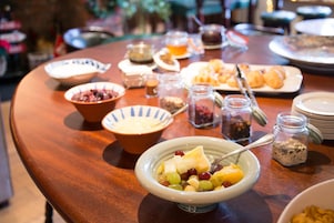 Uma mesa de buffet com diversos pratos, incluindo uma tigela de salada de frutas, um prato de doces e vários pequenos frascos de acompanhamentos.