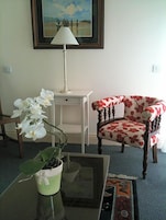 Quarto com uma cadeira, uma mesa, uma luminária e um quadro na parede.