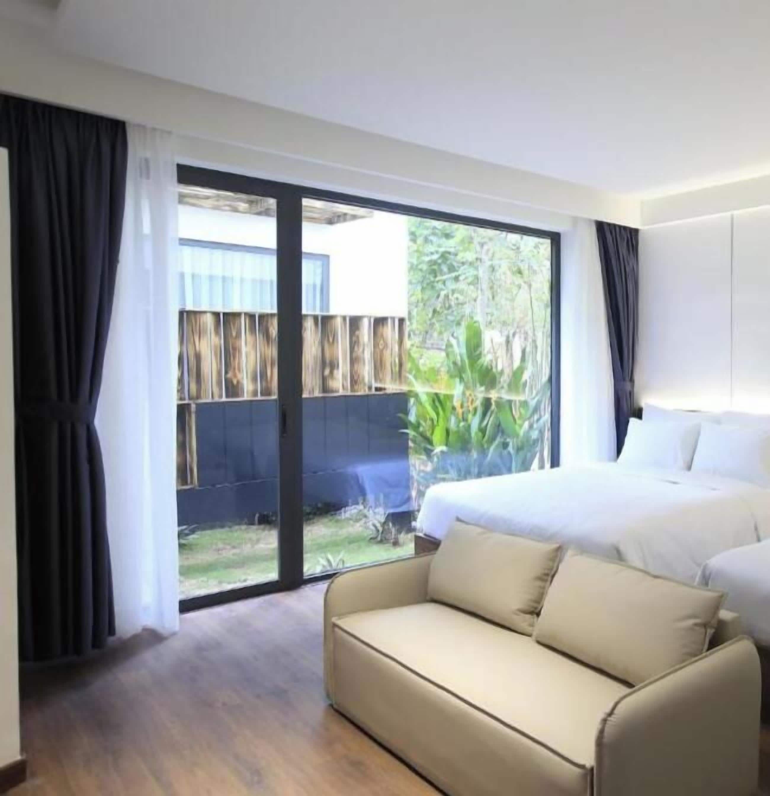 Quarto com cama, sofá e porta de vidro deslizante para um jardim.