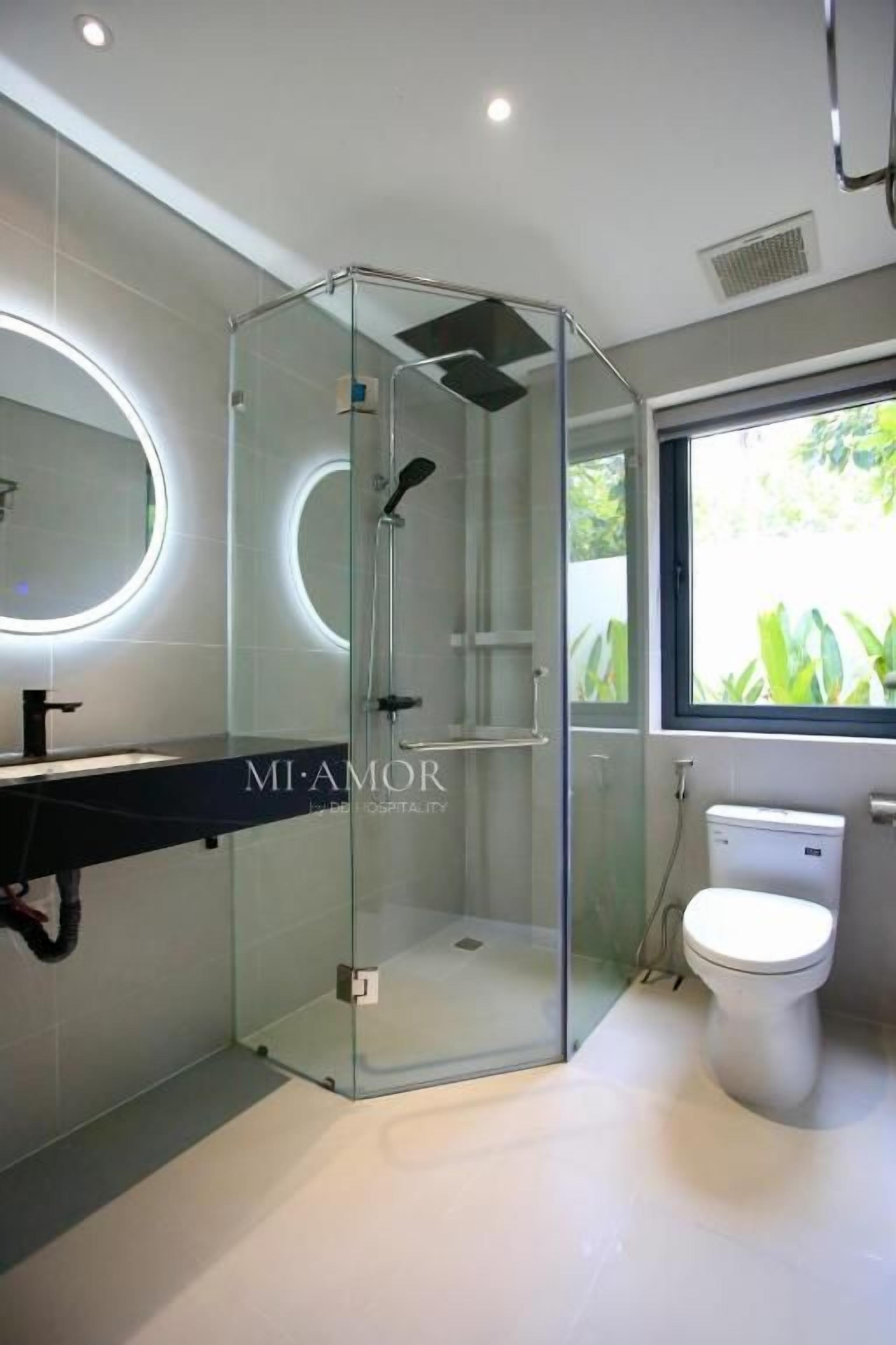 Casa de banho moderna com chuveiro envolto em vidro, sanita e toucador com espelho.