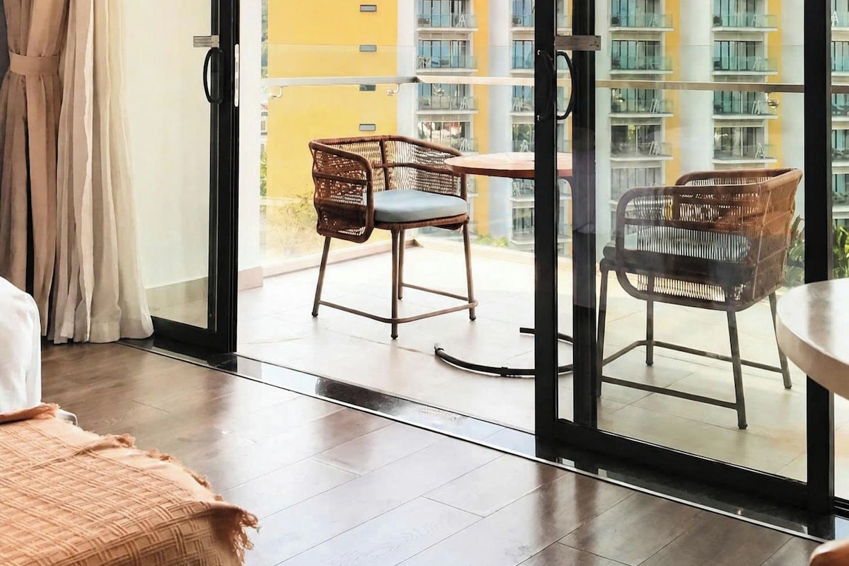 Quarto de hotel com porta de vidro deslizante que dá para uma varanda externa com mesa e cadeiras.
