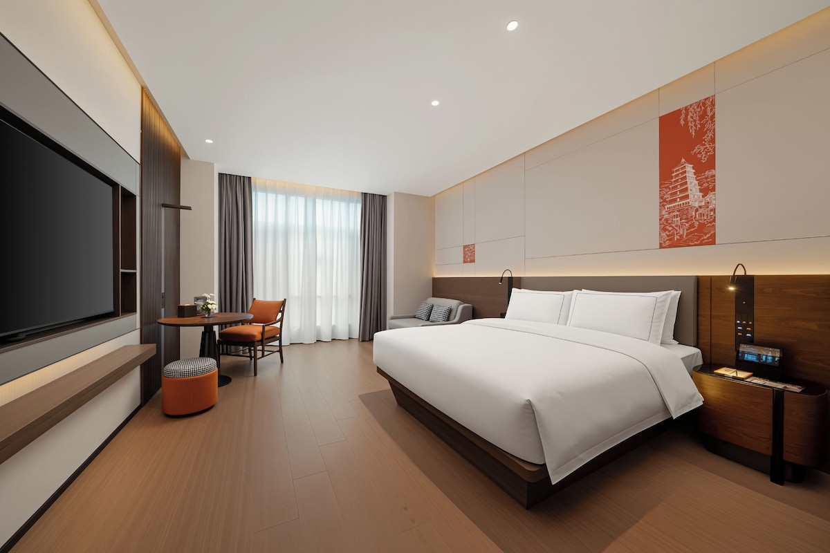 Quarto de hotel moderno com uma cama grande, televisão, escrivaninha e uma cadeira.