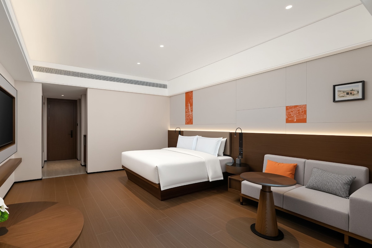 Quarto de hotel moderno com cama, sofá, mesinha e televisão.