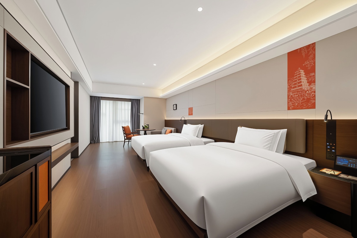 Quarto de hotel com três camas, uma televisão, uma escrivaninha e uma cadeira.