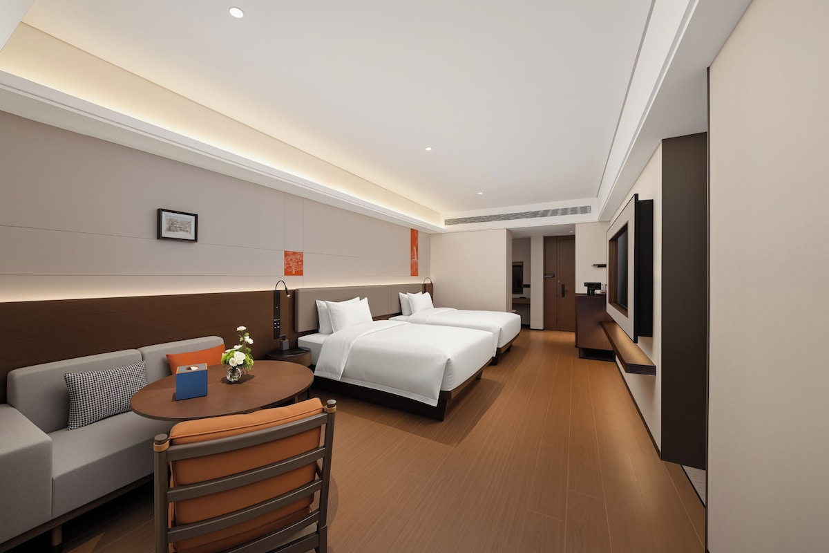Quarto de hotel com cama, sofá, mesa com um vaso de flores e televisão.