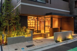 Entrada moderna de hotel com fachada de vidro, área de estar ao ar livre e placa indicando 'Sumy Asakusa South'.