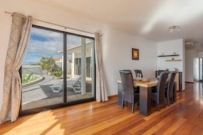 Uma área de refeições com uma grande porta de vidro deslizante que dá para um espaço ao ar livre, uma mesa de jantar com cadeiras e vista para o exterior.