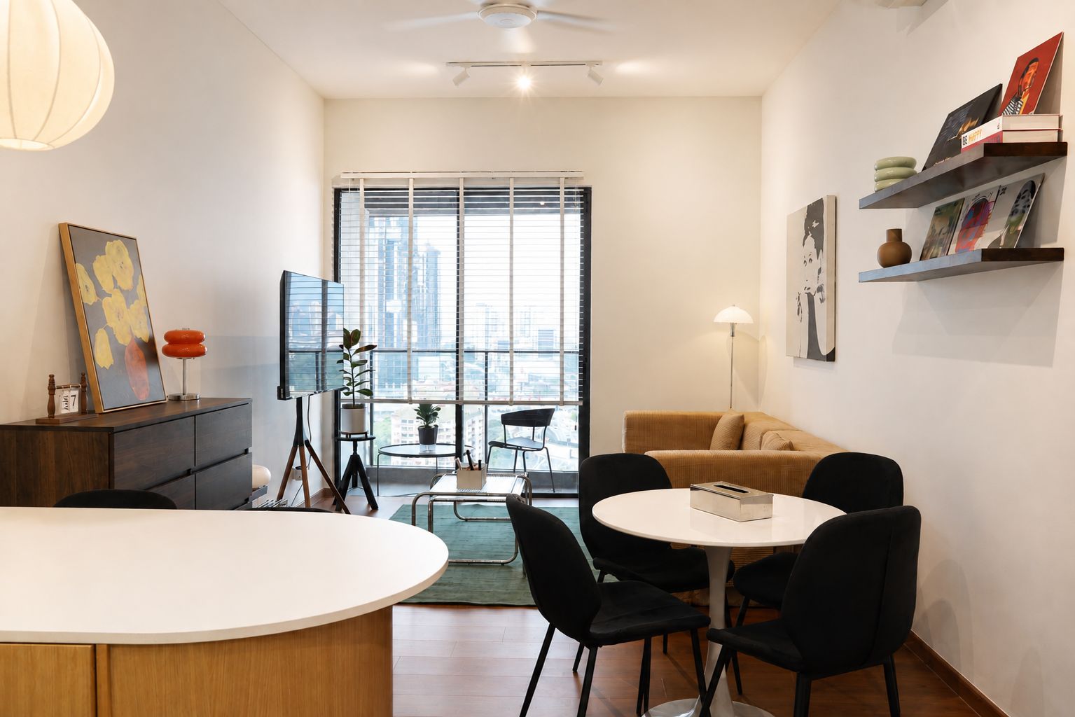 Uma sala de estar moderna com um sofá, uma mesa de jantar com cadeiras, uma TV e uma janela grande com persianas.