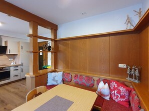 Espaço compacto living com cozinha compacta, área de refeições com mesa e cadeiras, e área de estar com almofadas e um banco.