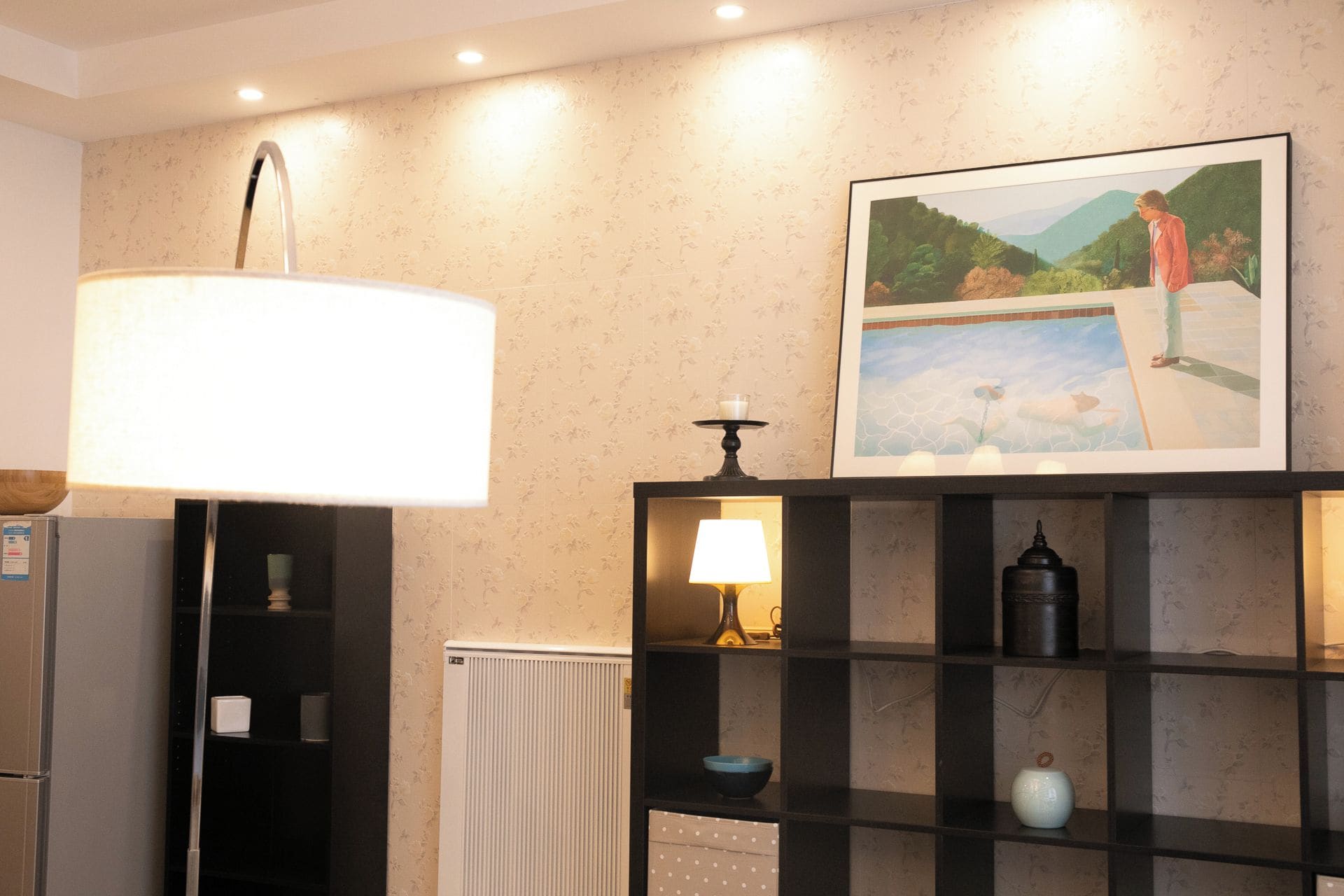 Quarto com radiador, prateleira com objetos decorativos, quadro pendurado na parede e luminária suspensa.